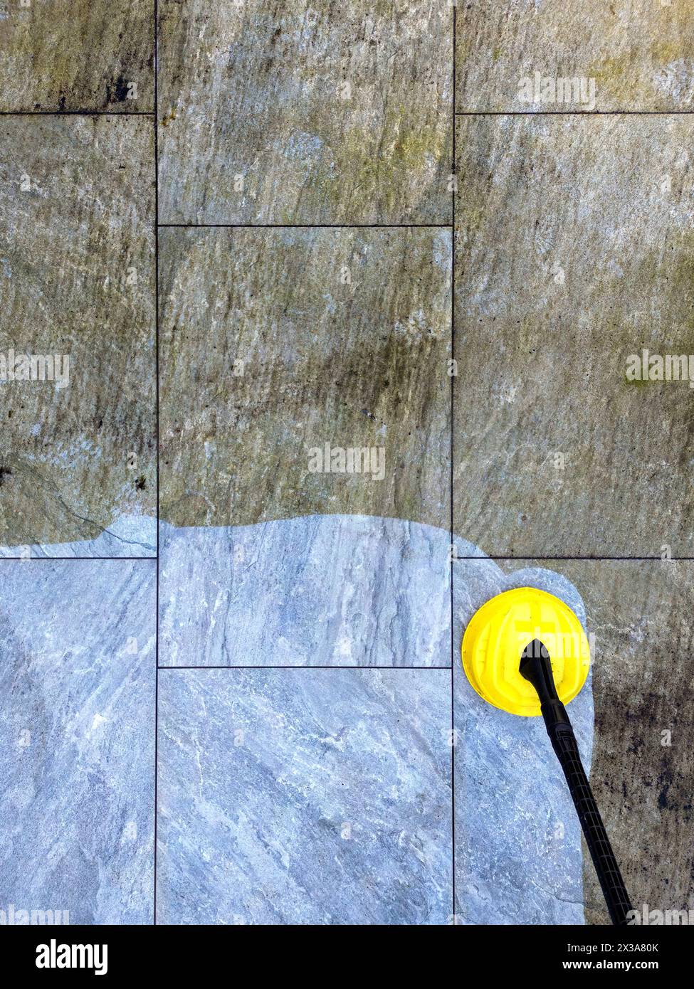 Pressure jet washer being used to clean porcelain tiles on a garden ...