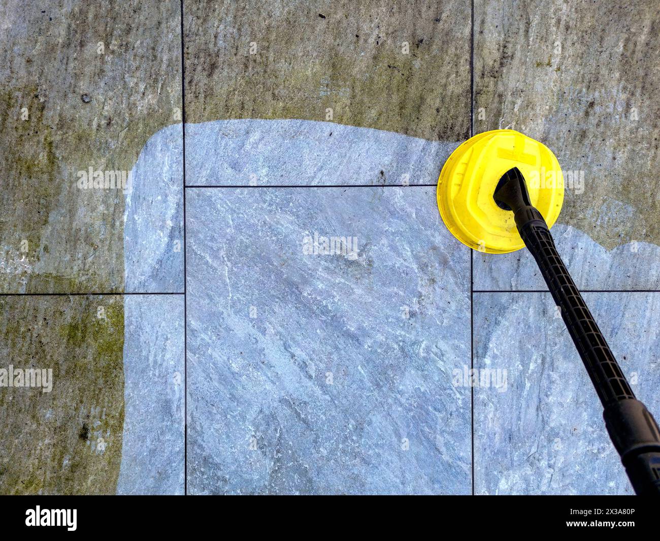 Pressure jet washer being used to clean porcelain tiles on a garden ...