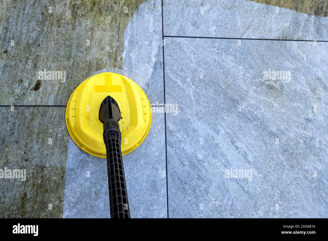 Pressure jet washer being used to clean porcelain tiles on a garden ...