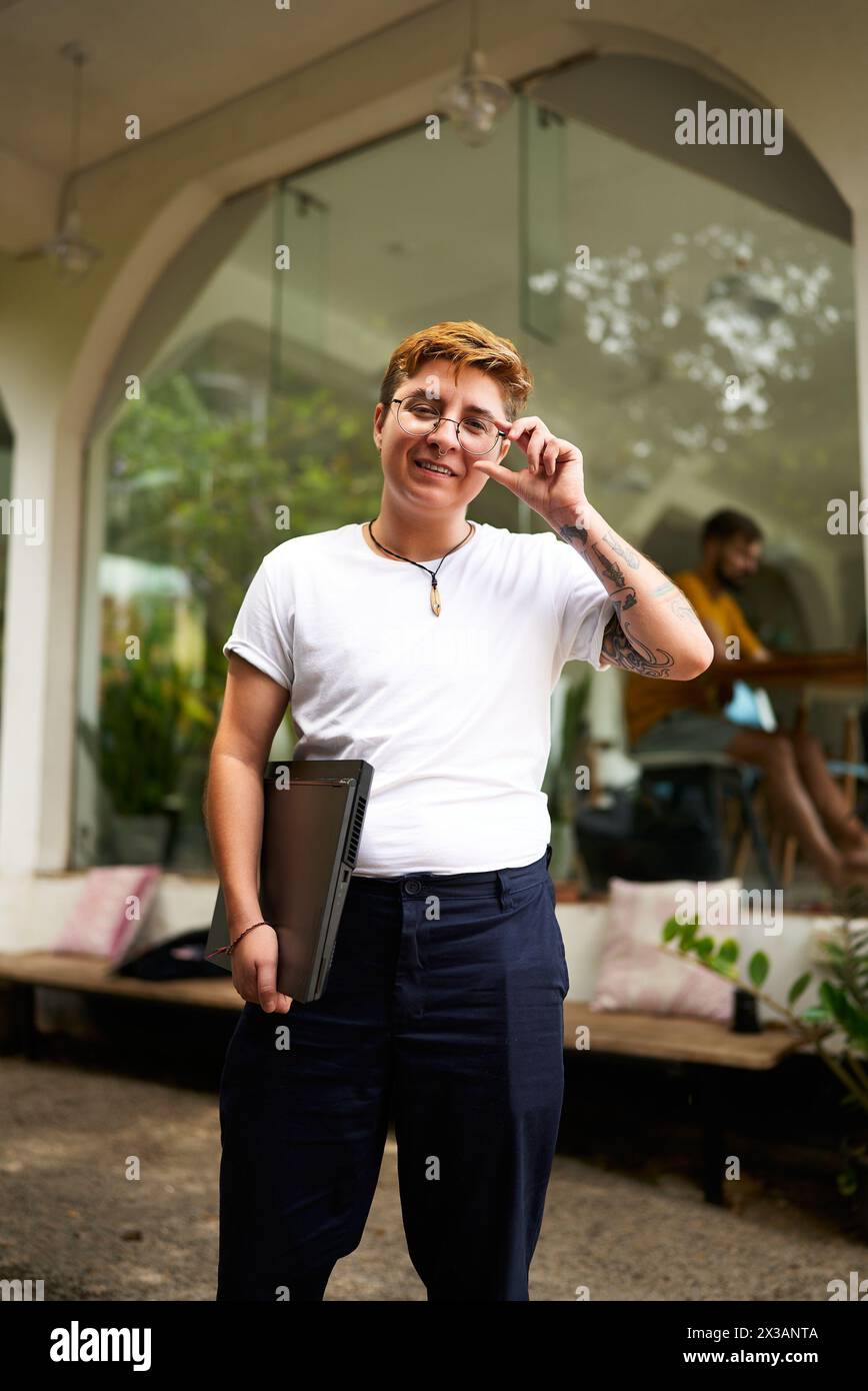 Transgender professional stands confidently in an office with laptop ...