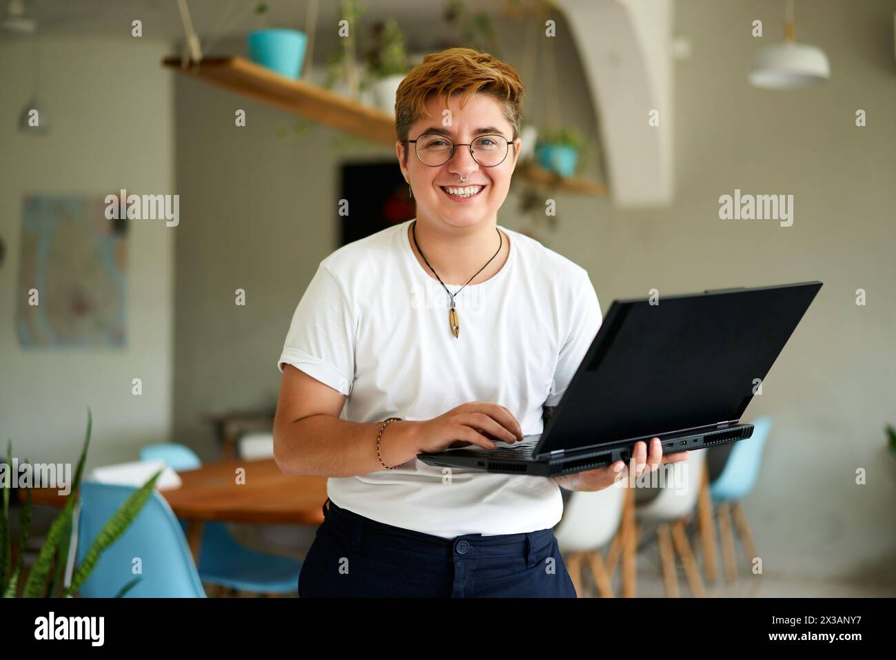 Cheerful transgender professional holds laptop, smiles in modern office ...