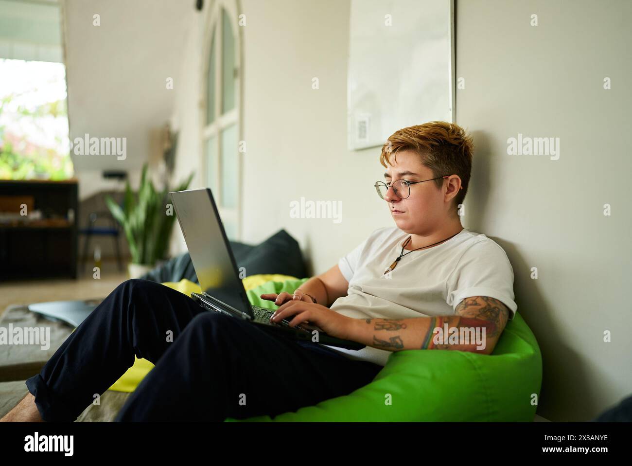 Transgender pro works on laptop from cozy bean bag in modern coworking ...