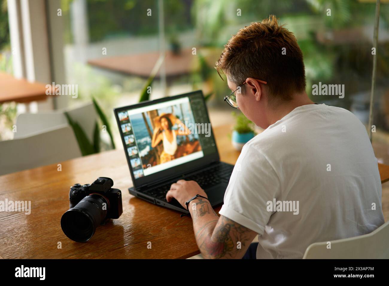 Focused photo editor with tattoos retouches images on laptop at ...
