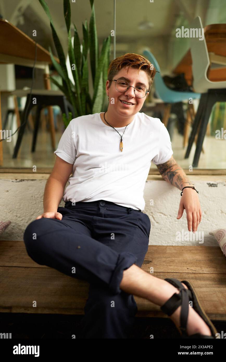 Smiling young transgender professional sits comfortably in modern ...