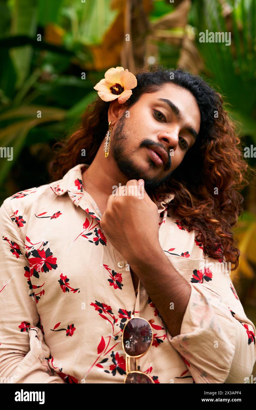 Confident ethnic man with flower in hair poses, tropical background ...