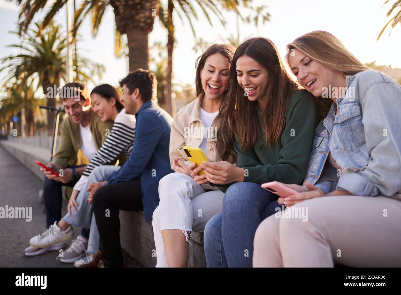 Large and diverse group of gen z friends smiling sitting outdoors using ...