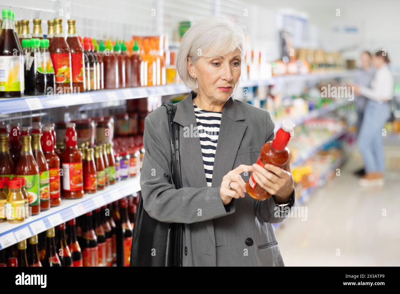 Aged woman reading labels on bottles with sauces in supermarket Stock ...