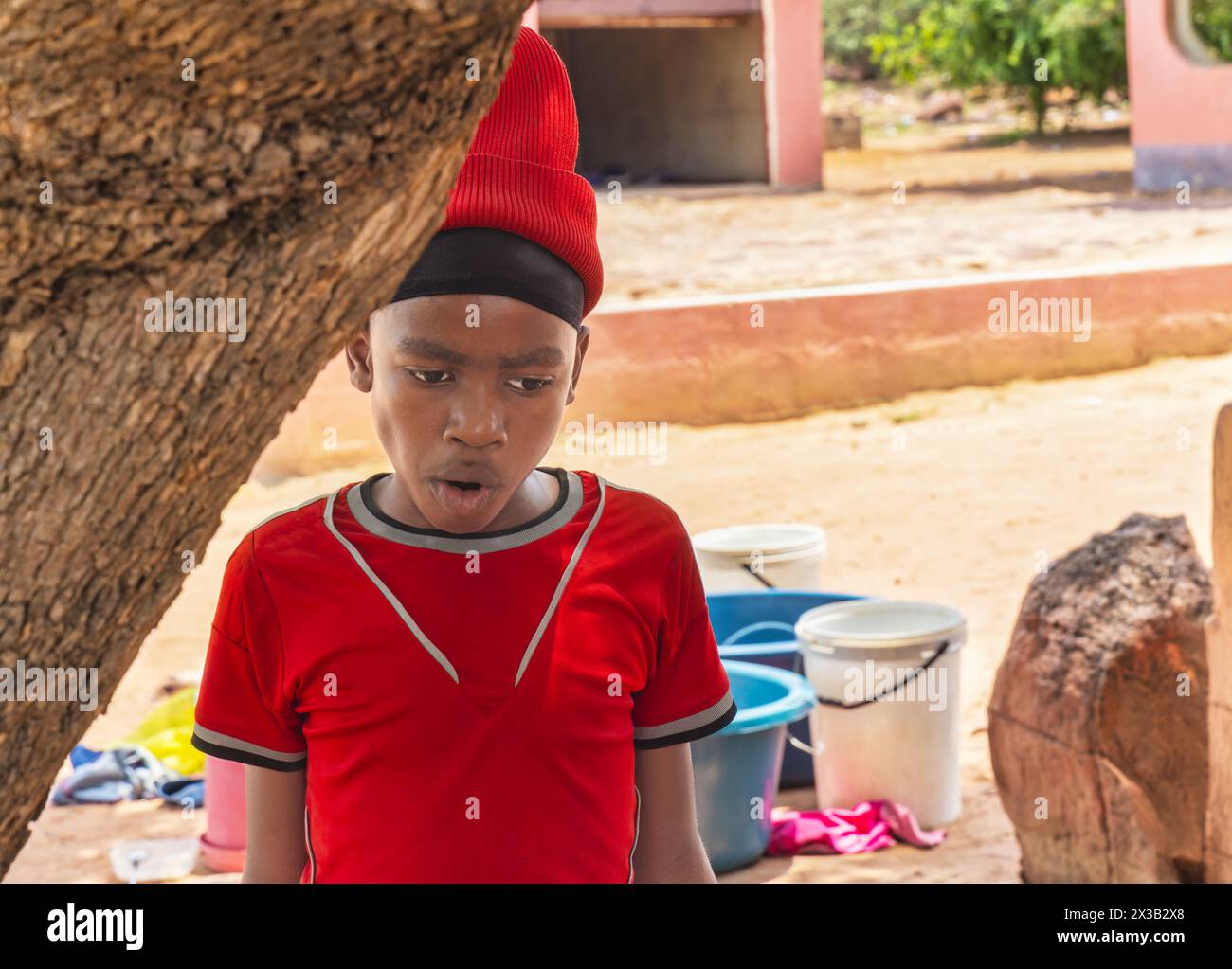 village african teenager boy , wearing a red beanie , standing in front ...