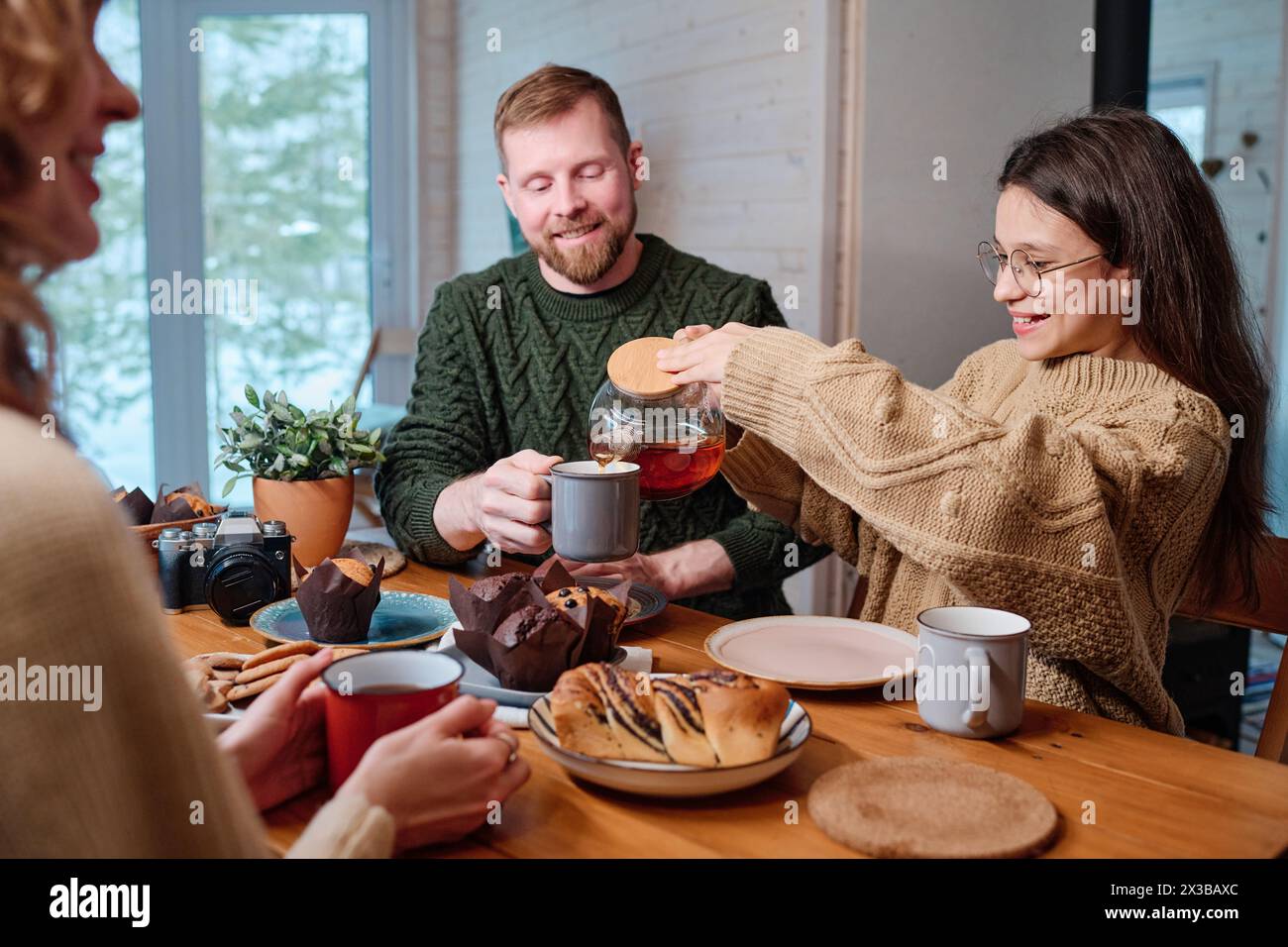 Caucasian teen girl pouring tea into mug for her dad during family meal ...