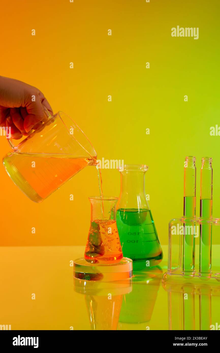 Hand model holding a cup pouring orange liquid into a small erlenmeyer ...