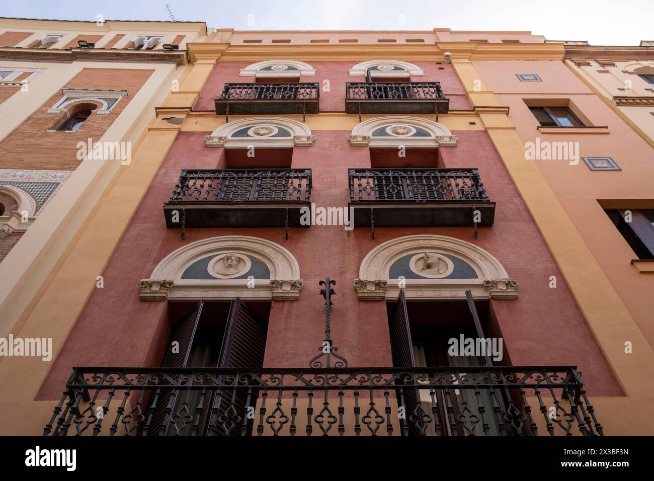 Red building facade featuring balconies with ornamental arches above ...