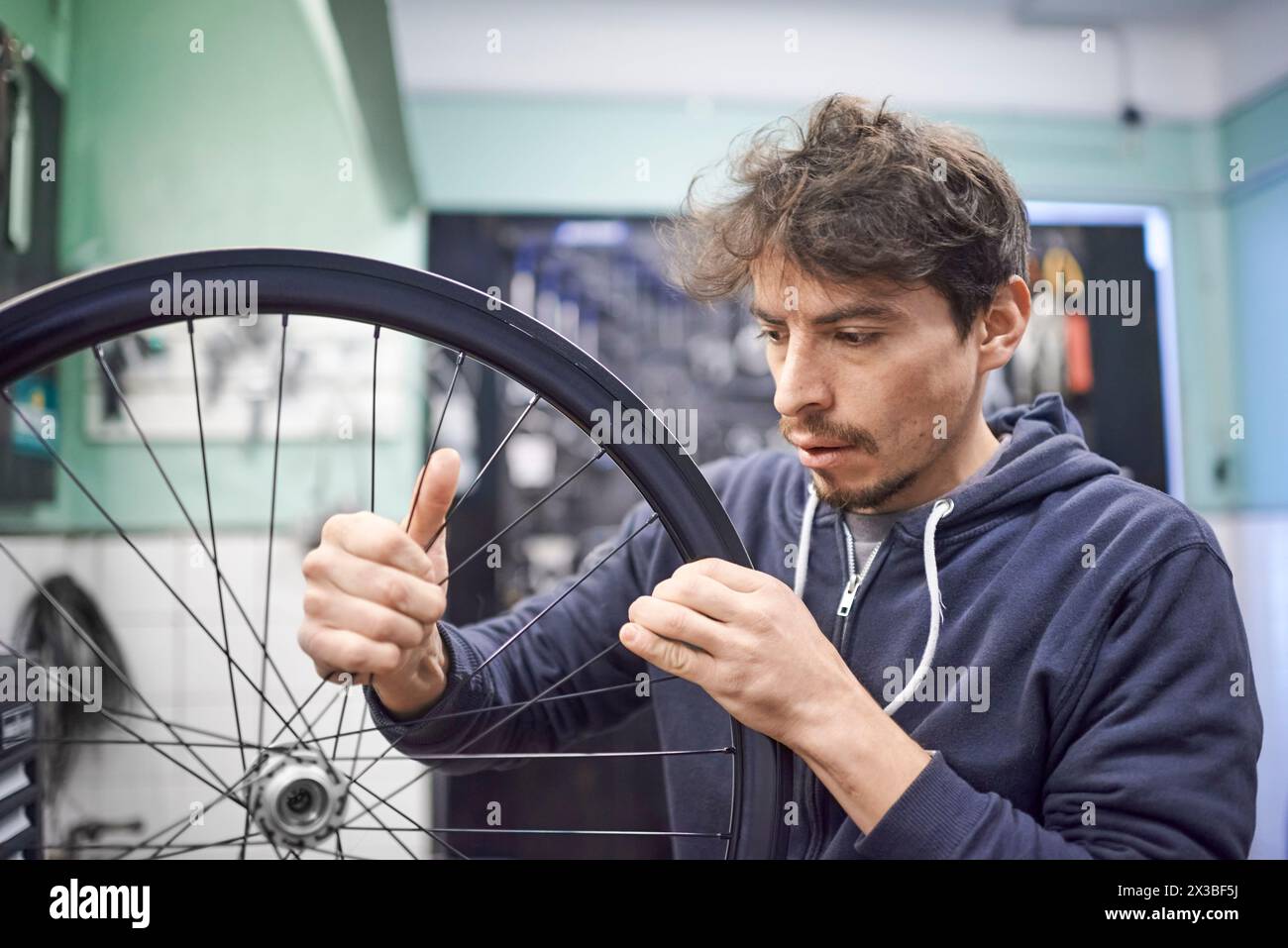 Young hispanic man checking the tension of the spokes of a bicycle ...