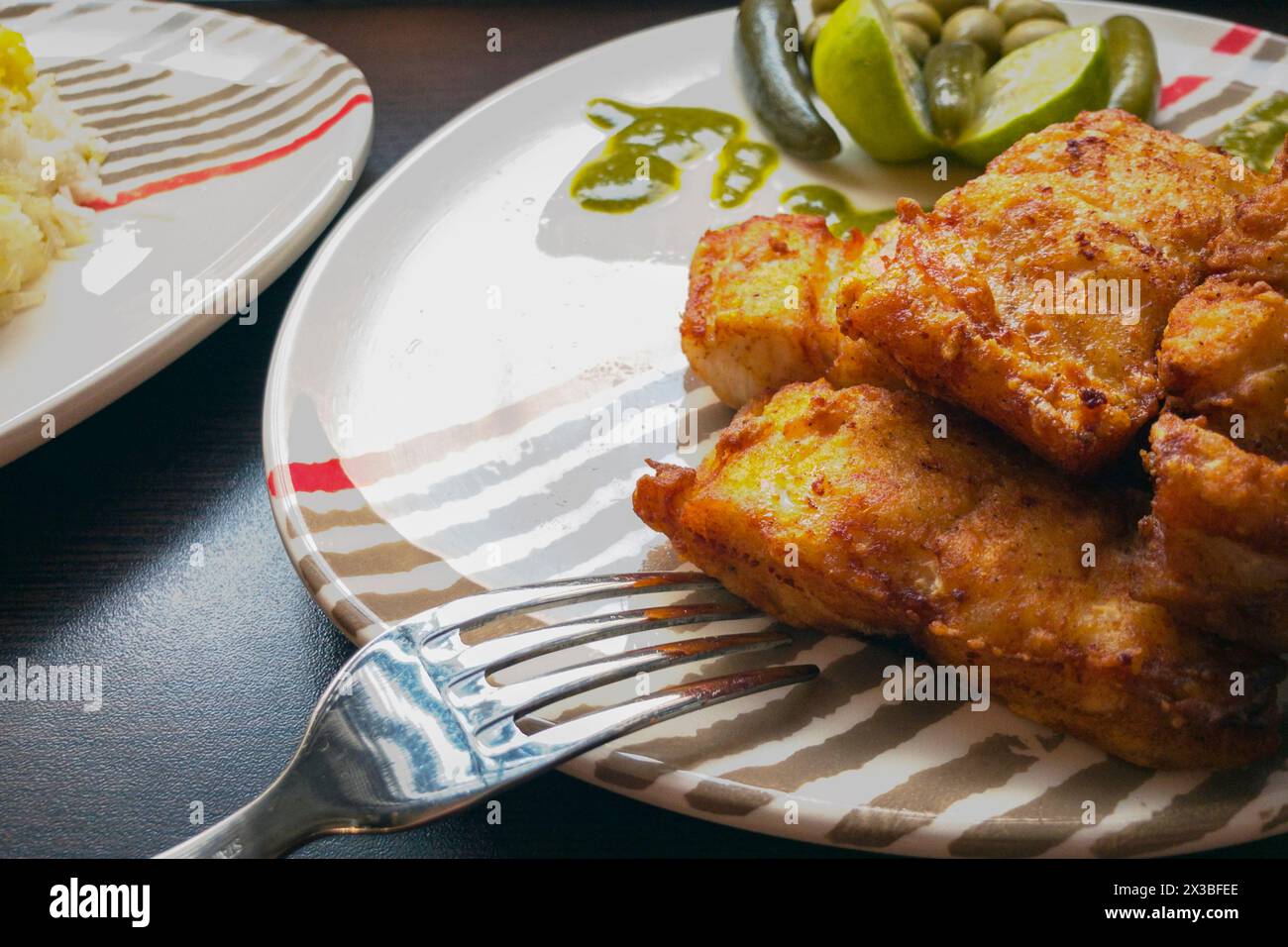 Delicious fried fish served on a plate. It has olives and pickles on ...