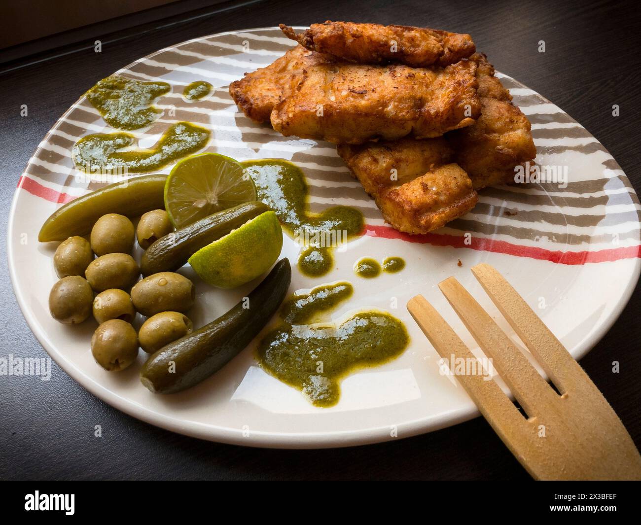 Delicious fried fish served on a plate. It has olives and pickles on ...