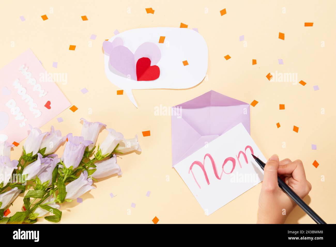 Hand model holding a black pen writing a word “Mom” on a card. A bunch ...