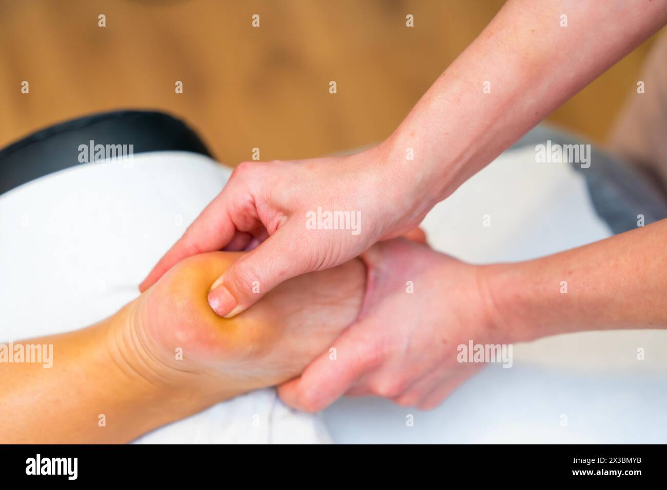 Close-up of the hands of a professional massage therapist giving a reflexology foot massage to a ...