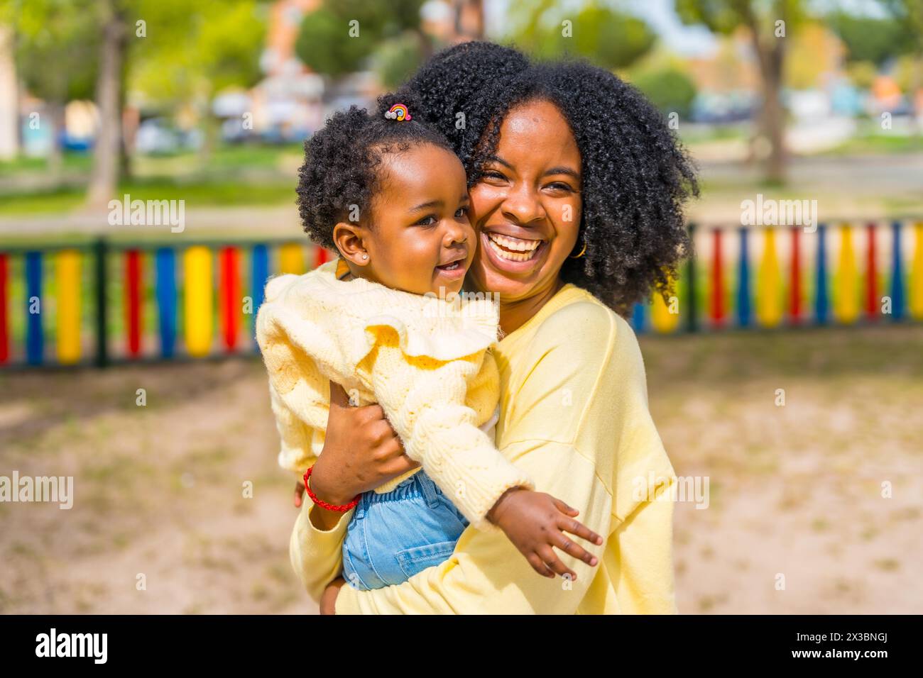 Happy african american mother embracing and holding in arms her little daughter on a park Stock ...