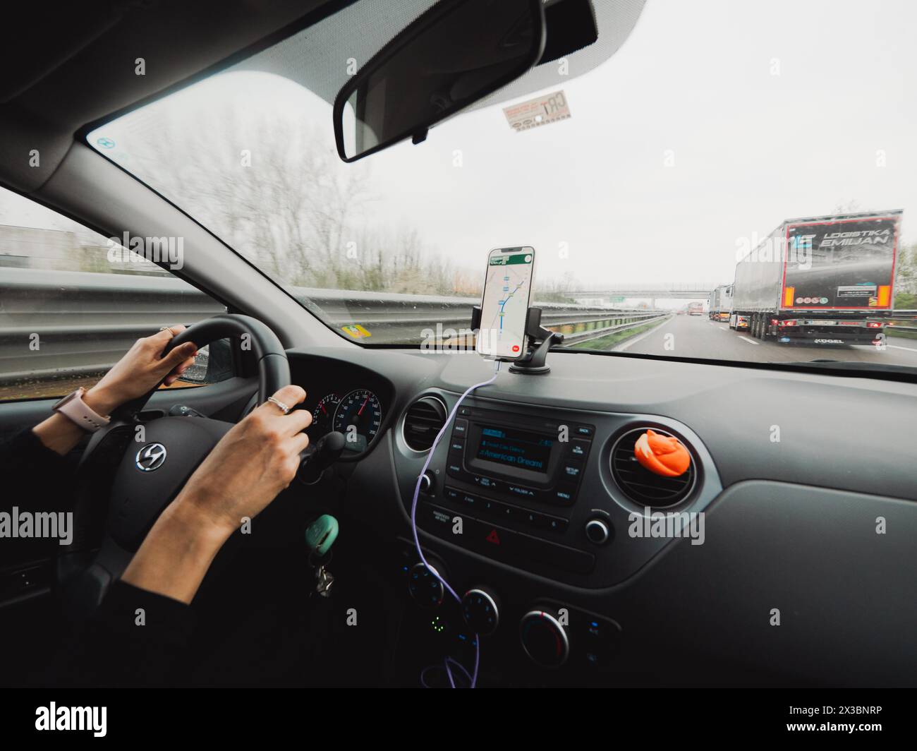 Inside view of a car with the driver's hands on the wheel and a mobile ...