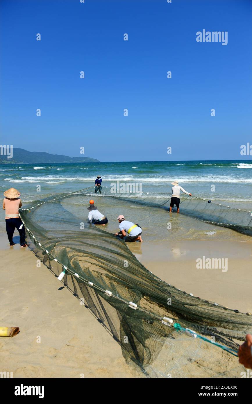 Vietnamese fishermen pulling out a large fishing net from the beach in ...