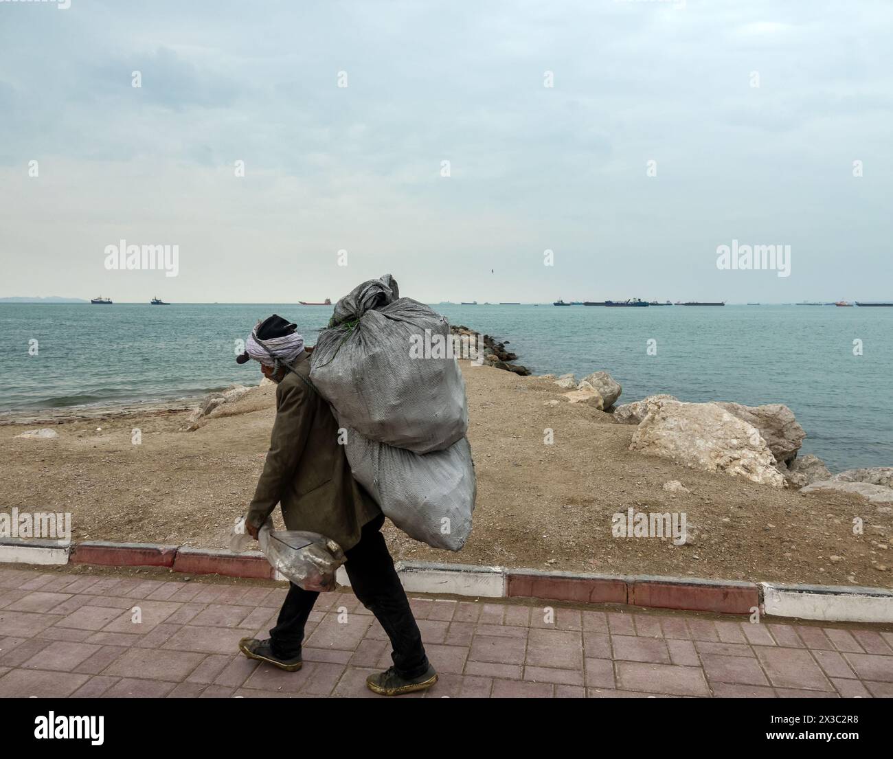 Bandar Abbas, Iran- January 9, 2023: A homeless man with a bag walks ...