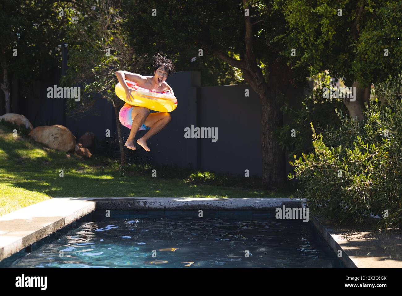 A teenage Asian boy is jumping into a pool with a colorful float ...