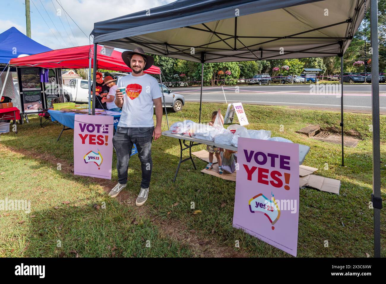 A young man wearing an Akubra hat stand smiling at a Vote Yes campaign ...