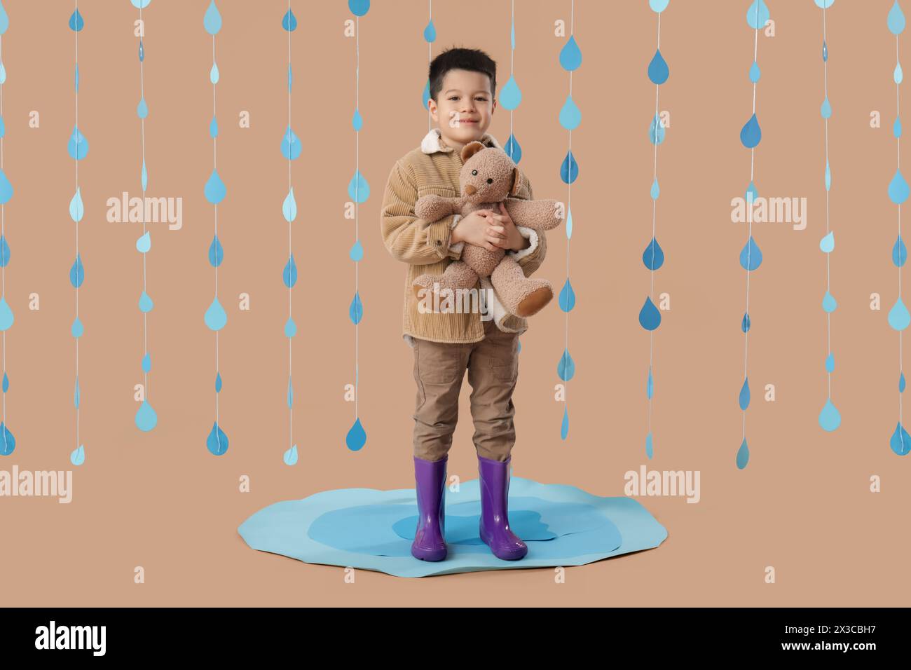 Cute little Asian boy with toy bear and raindrops standing in paper ...