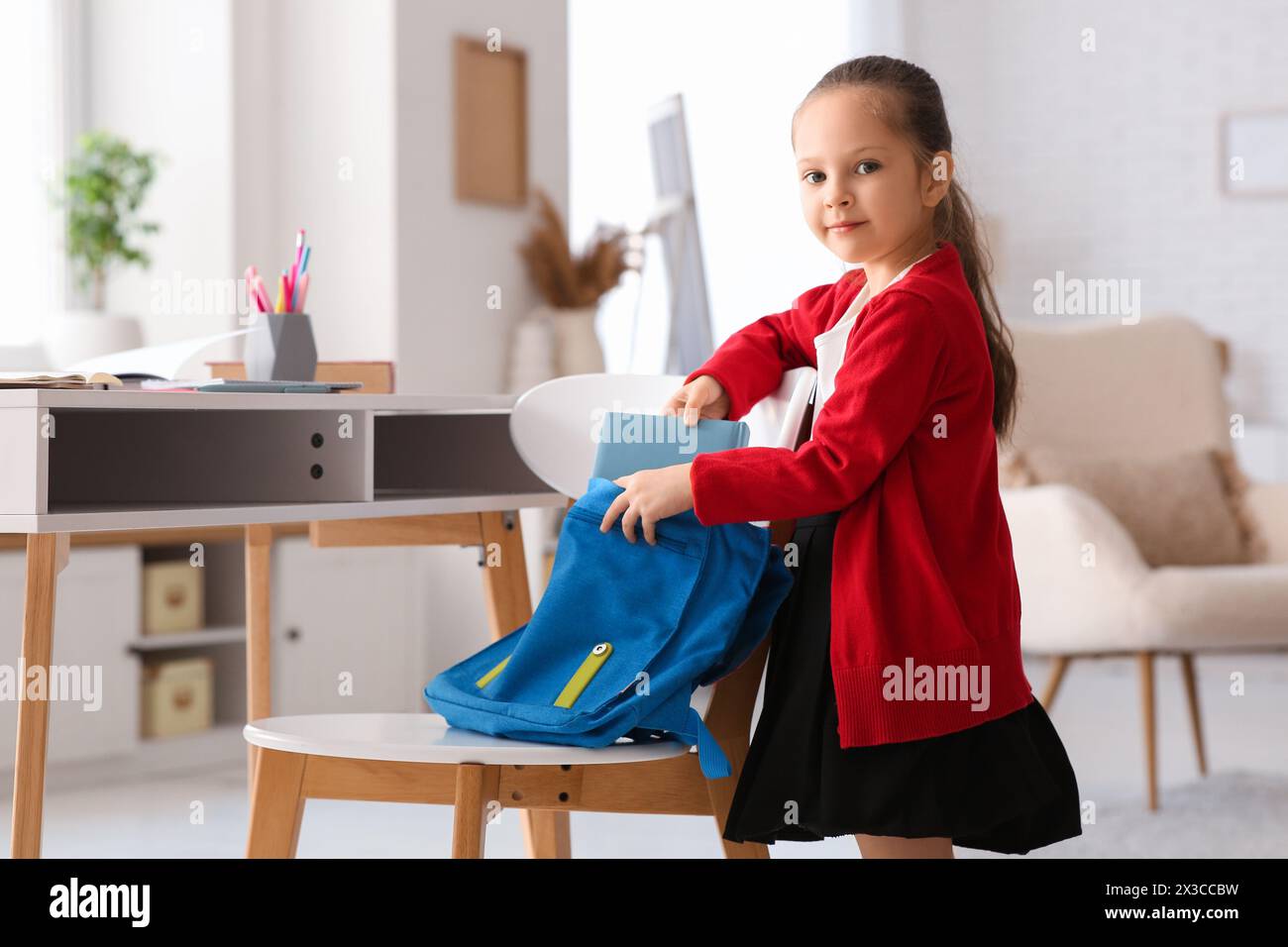 Cute little girl putting book in backpack at home Stock Photo - Alamy