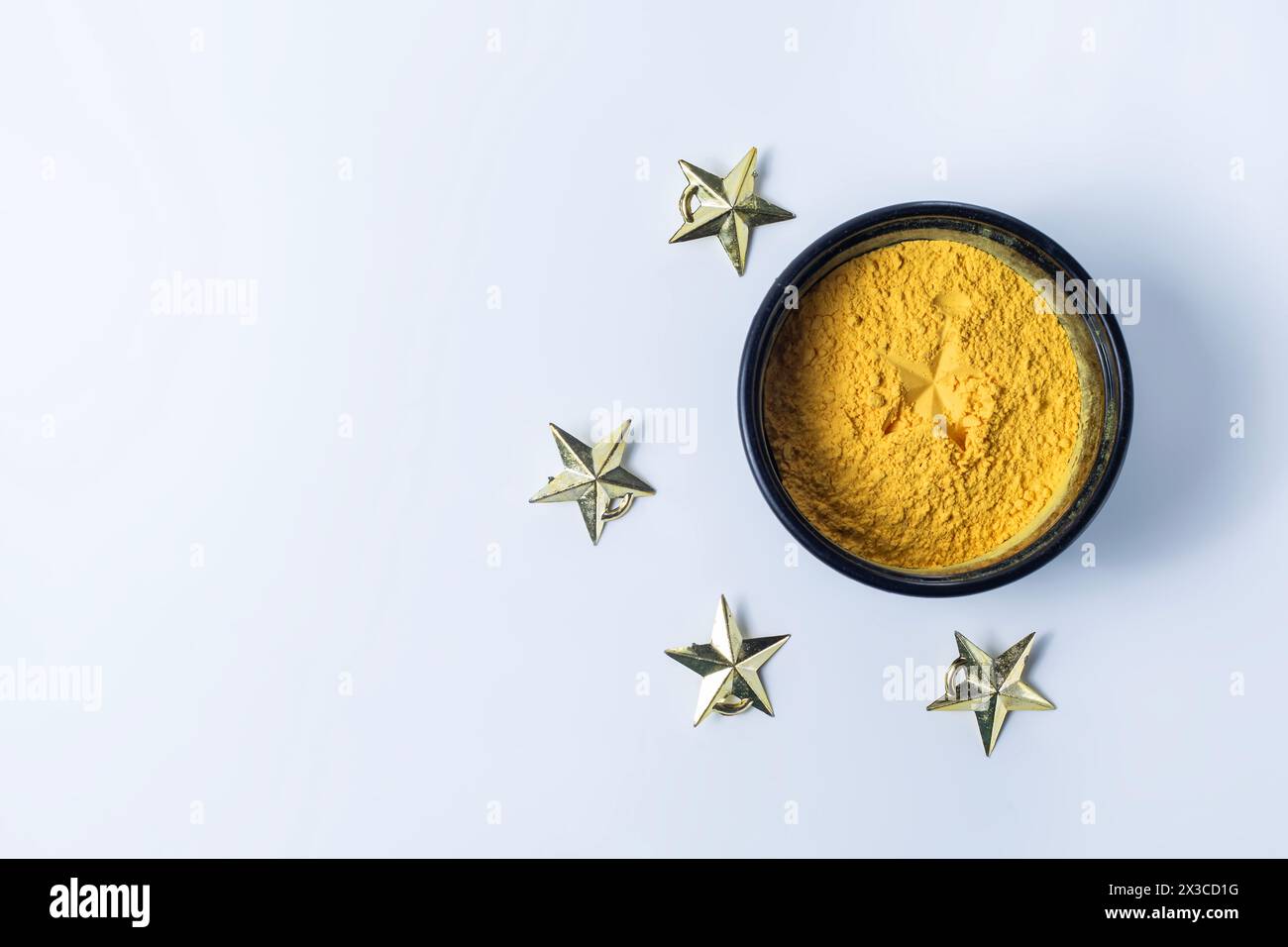 Yellow color holi powder in a bowl with golden stars on white ...