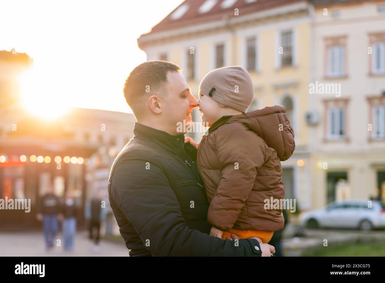 A happy father and three year old son hug in a city street. Warm ...