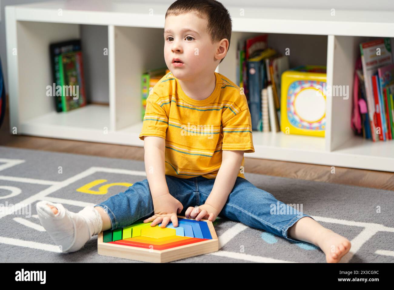 Toddler boy with a bandage or cast on his leg plays with wooden blocks ...