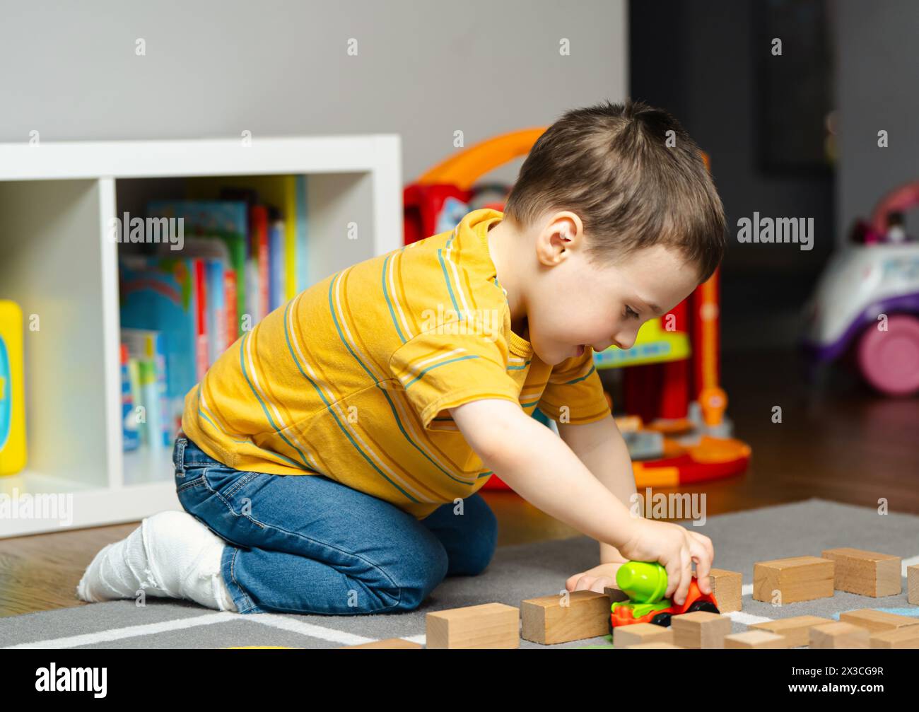Toddler boy with a bandage or cast on his leg plays with toys and ...