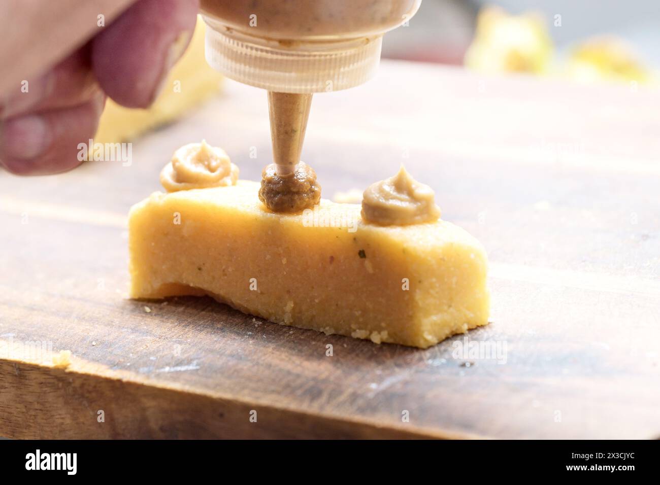 Chef spreading bean puree from a squeeze bottle onto a strip of polenta ...