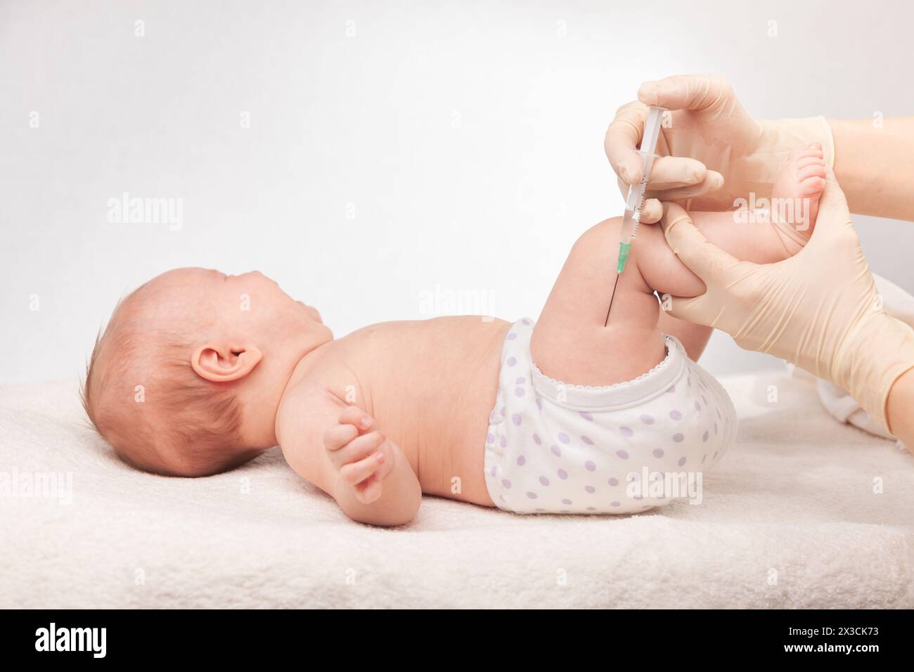 Baby receives a vaccination from a healthcare professional. Gloved ands ...