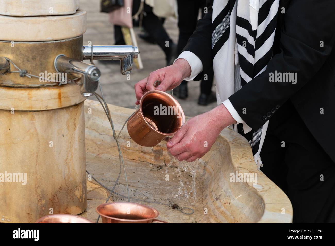 Closeup of a man using a copper natla or Jewish ritual hand washing cup ...