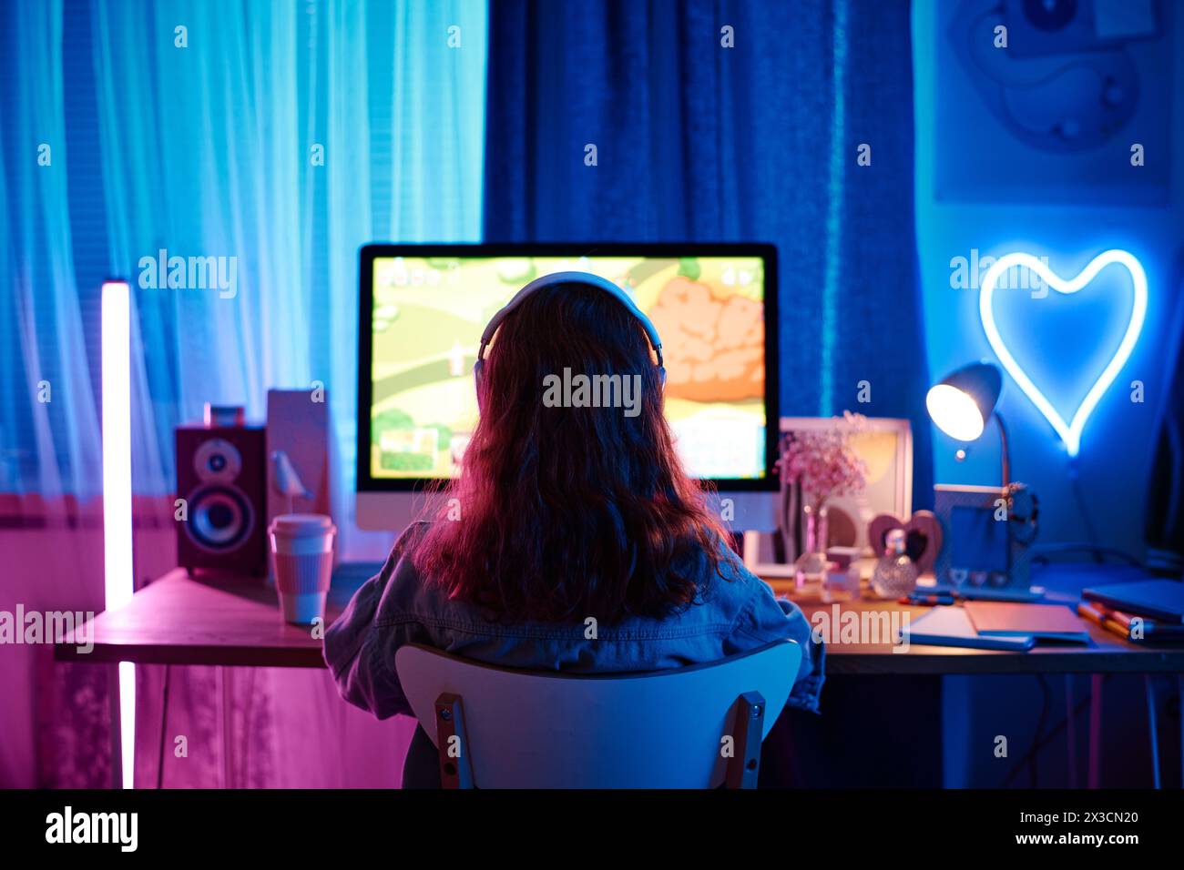 Rear view of unrecognizable girl wearing headphones sitting at desk in ...