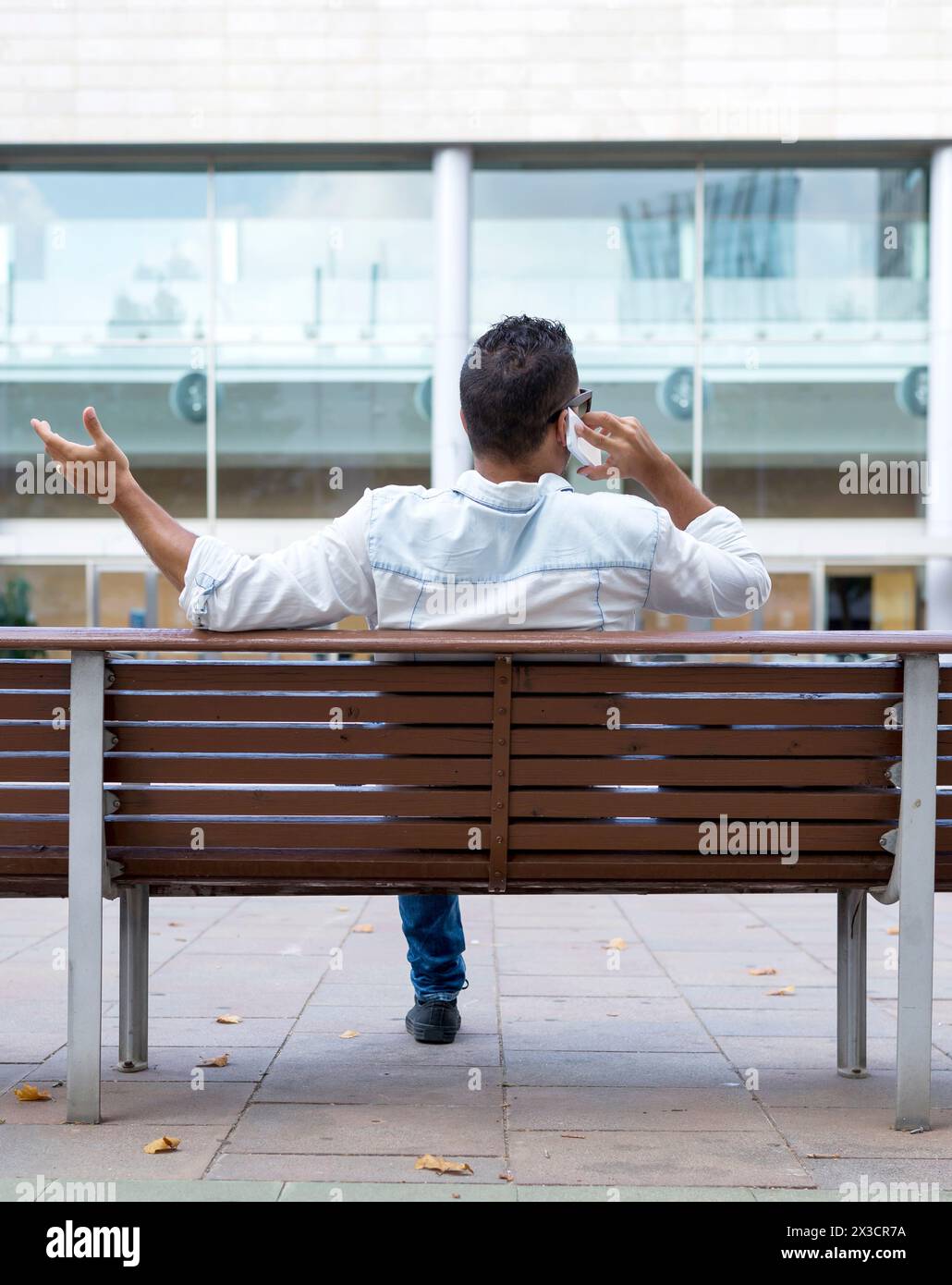 View from behind of a man sitting on a bench, gesturing while on a ...