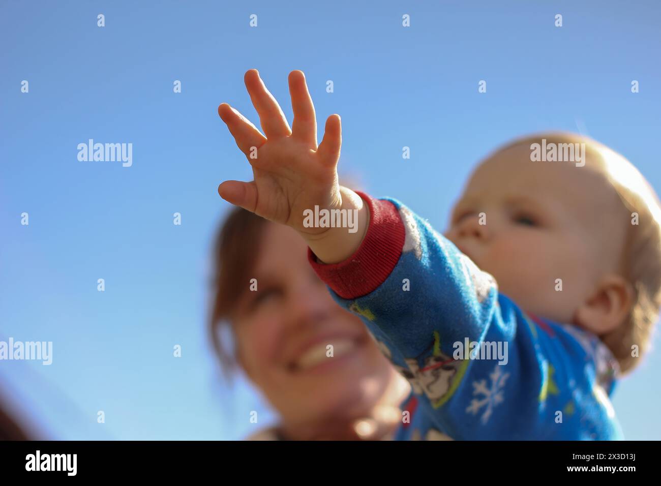 Baby reaching out under a blue sky, mother smiling behind Stock Photo ...