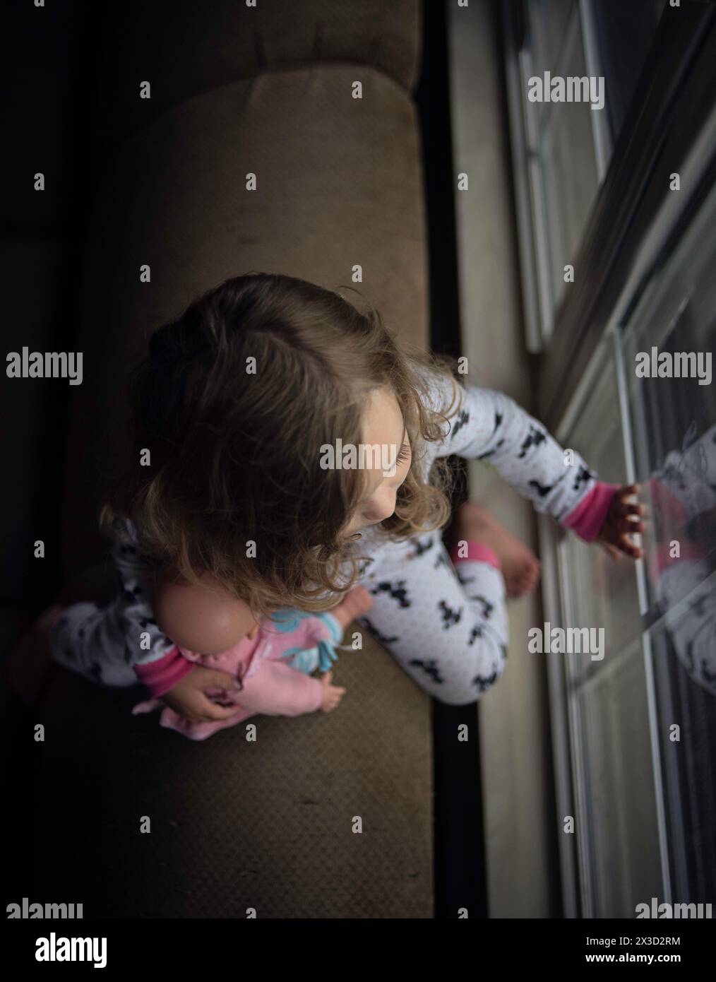 Little girl holding doll looking out window in pajammas Stock Photo - Alamy
