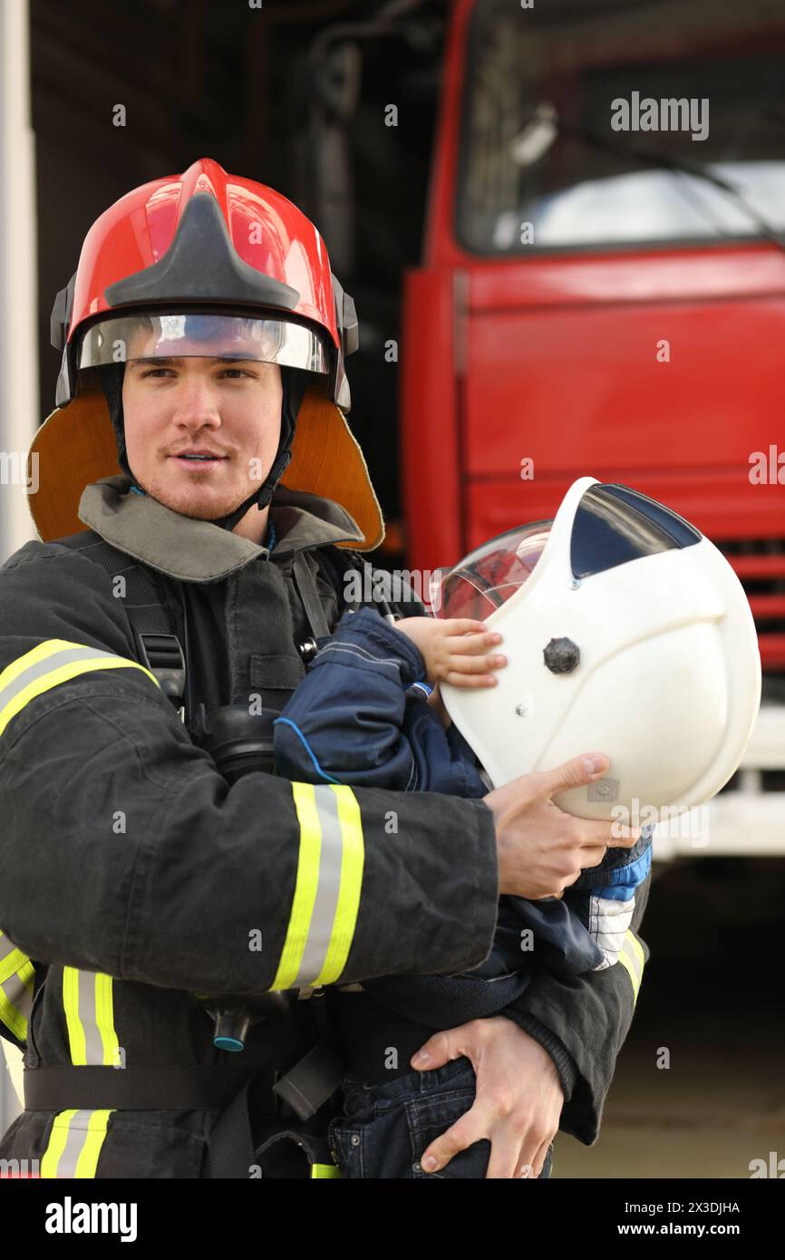 Portrait of fireman wearing fire fighter turnouts holds child in his ...