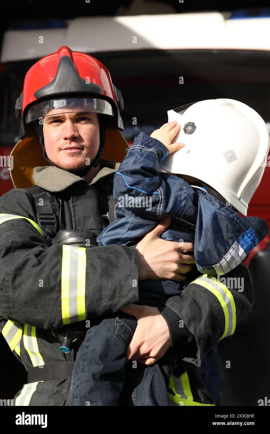 Portrait of fireman wearing fire fighter turnouts and red helmet, holds ...