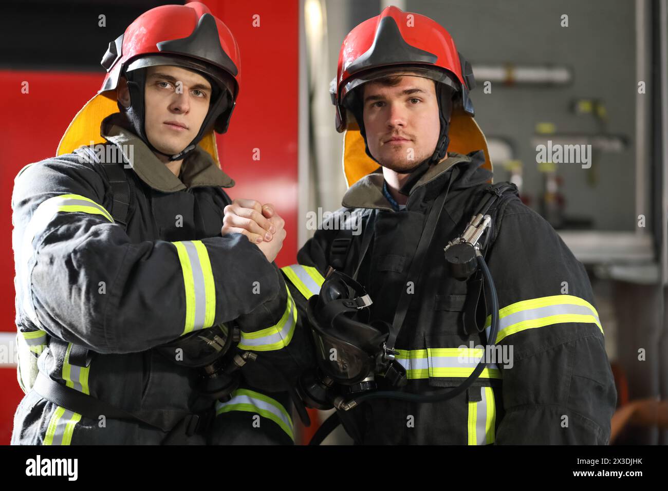 Two firefighters in protective clothing in helmets with fire engine ...