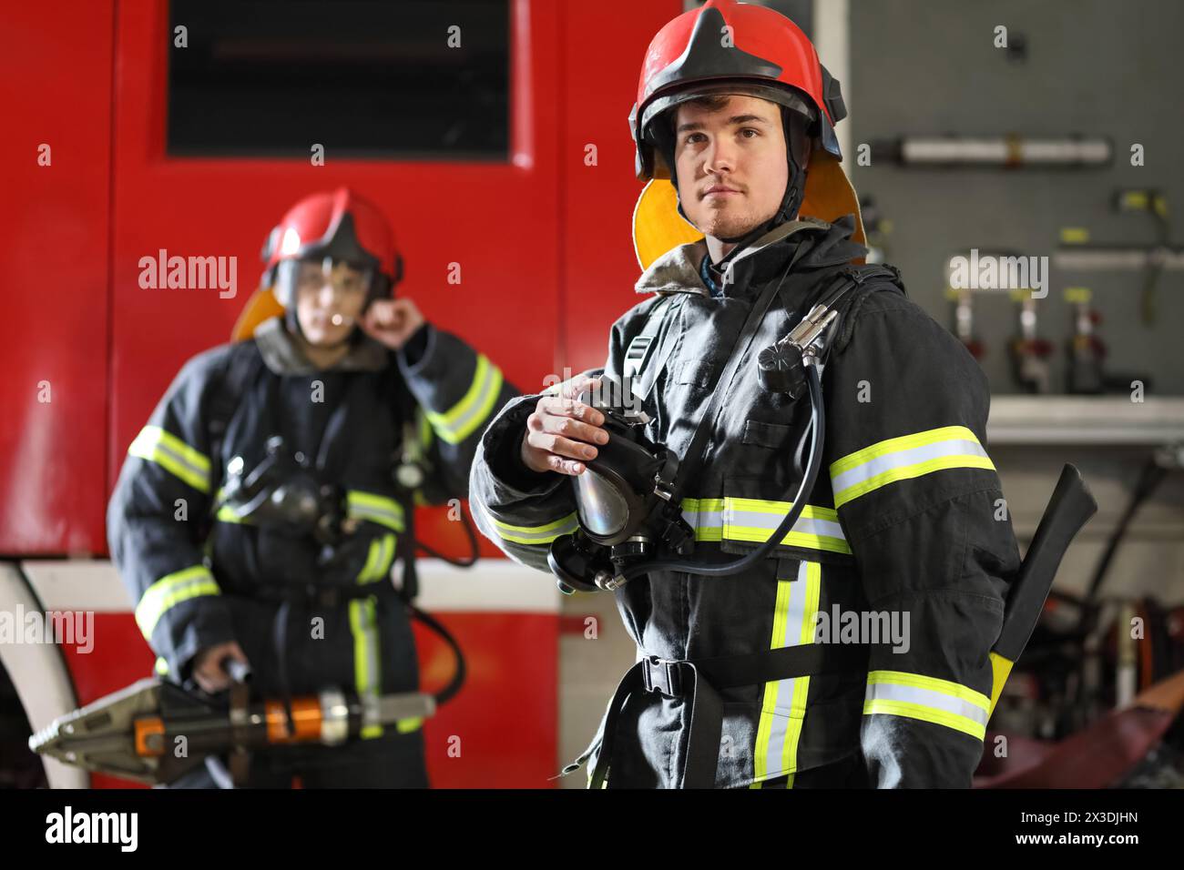 Two firefighters in protective clothing, helmets and rescue tool ...