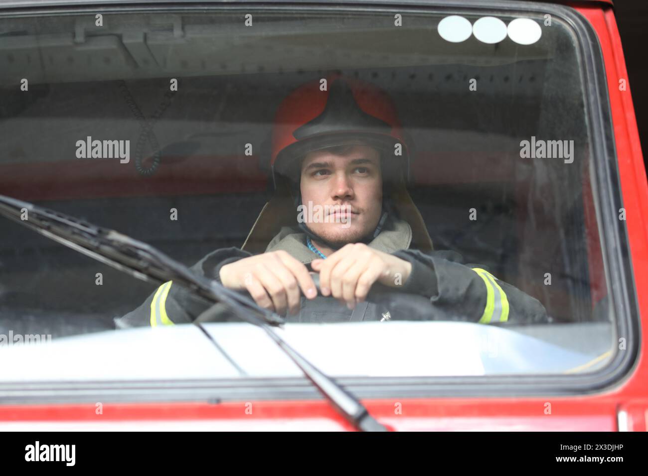 Portrait of fireman wearing fire fighter turnouts, sits behind wheel of ...