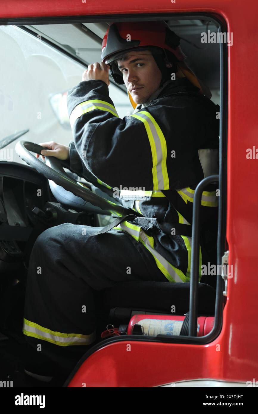 Portrait of fireman wearing fire fighter turnouts, sits behind wheel of ...