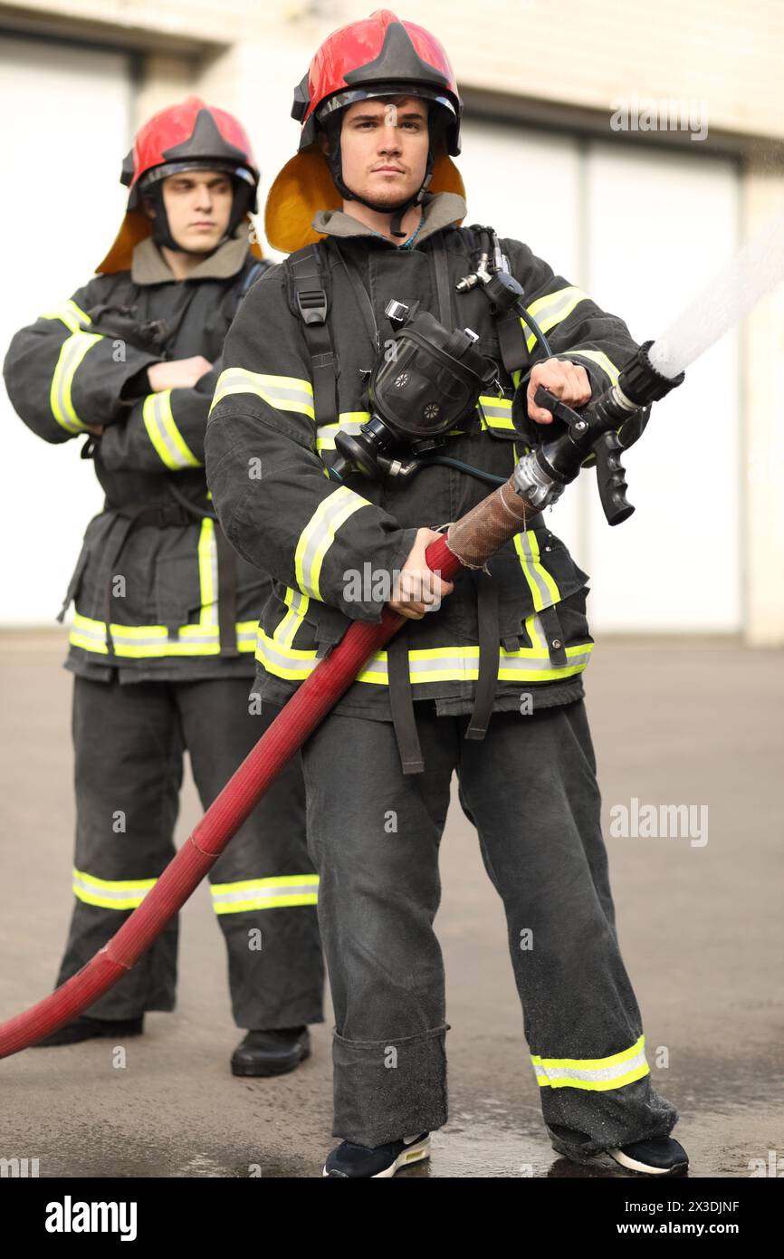 Portrait of two heroic fireman holds and adjust nozzle and fire hose ...
