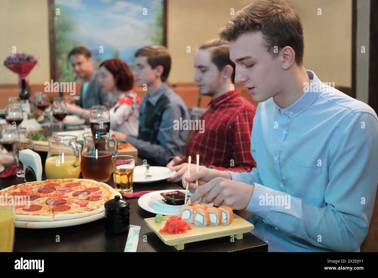 sitting guests invited to feast eat at table, young man in foreground ...