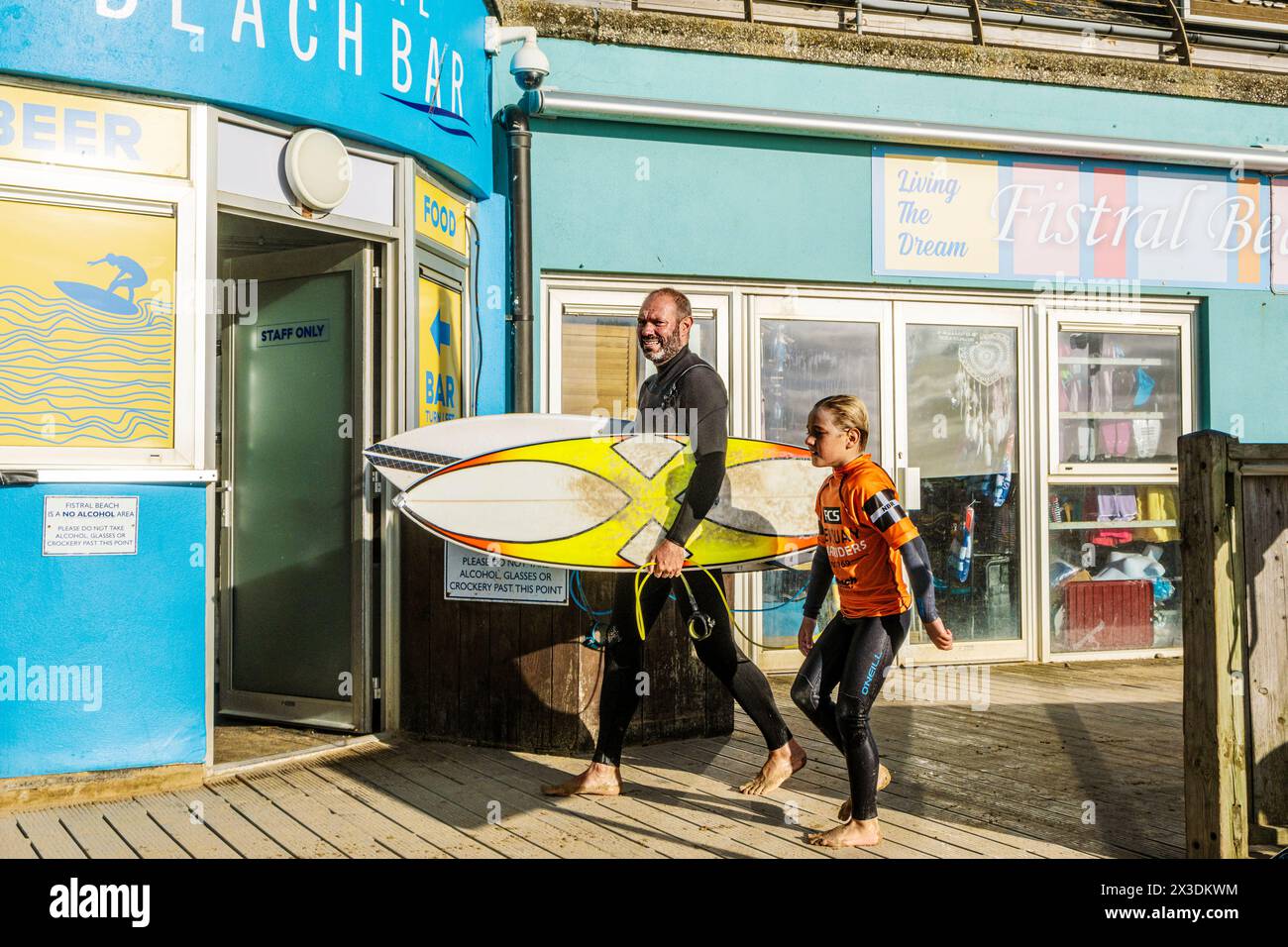 A father and son carrying surfboards and walking past the Fistral Beach ...
