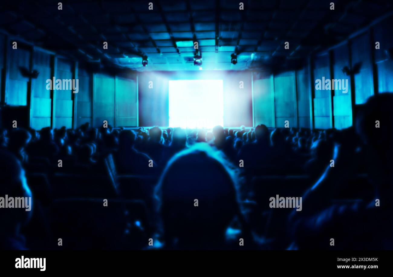 silhouette of people sitting in dark cinema hall, blue glow from screen ...