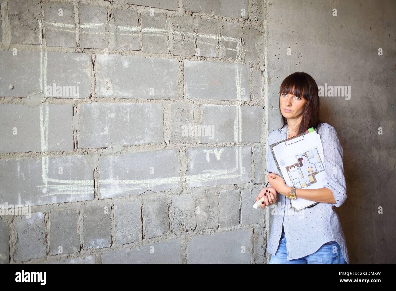Designer with piece of chalk and floor plan standing near the concrete ...